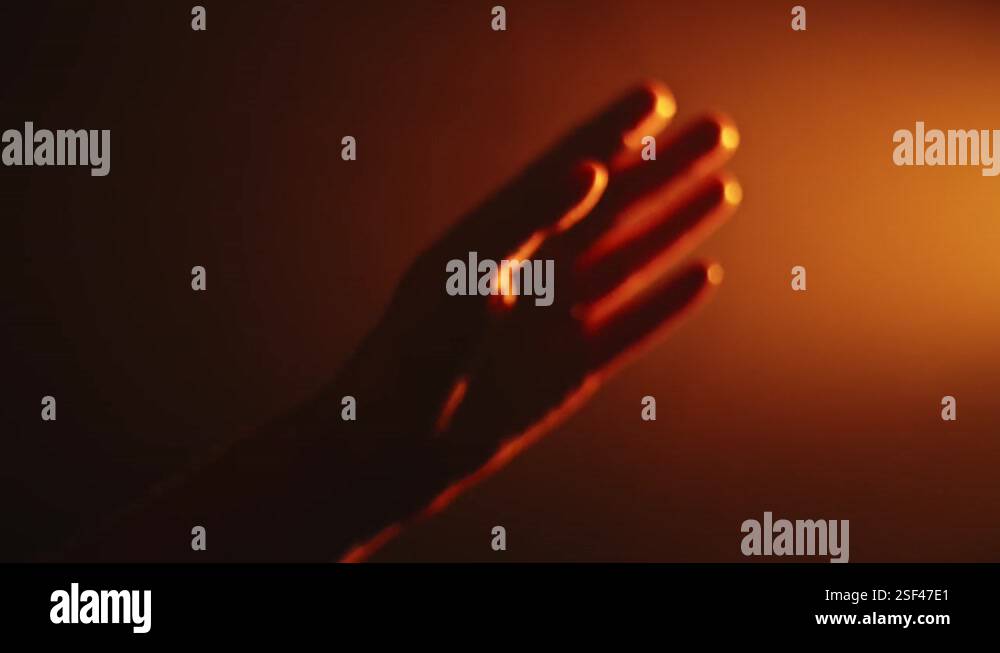 hand moving in front of a bright orange light source in a dark scenery ...