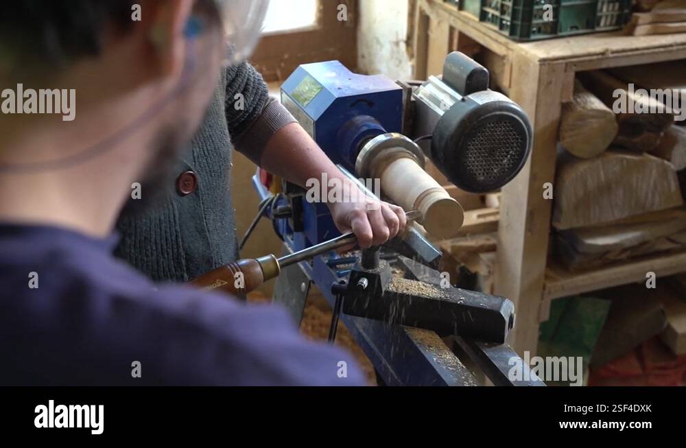 Carpenters shaping and shaving a beam of wood to a round shape with a ...