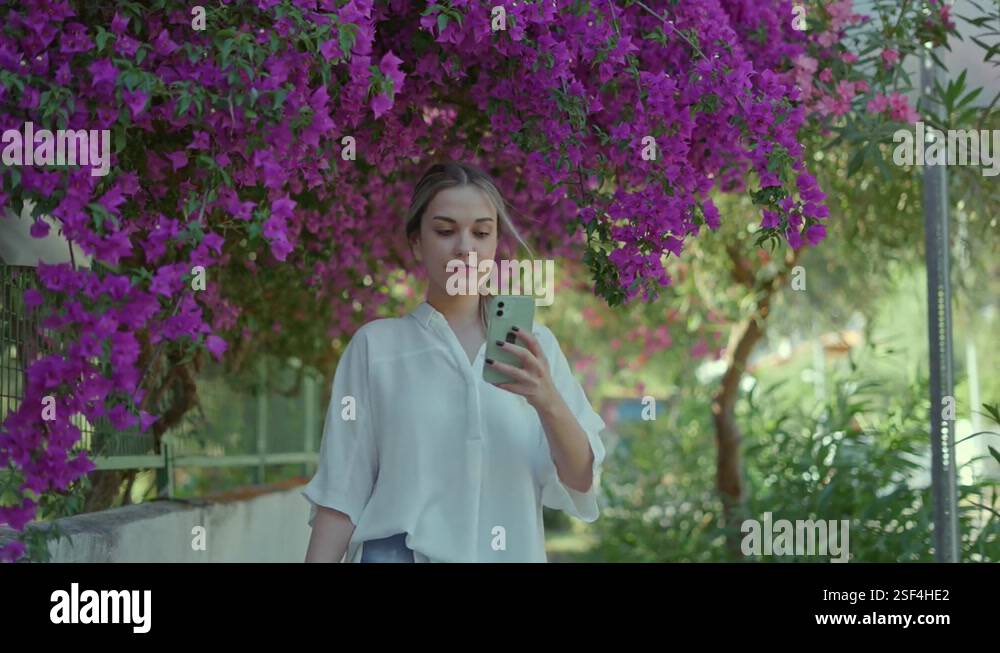 Teenage girl walks under a flowering tree and takes a selfie with her ...