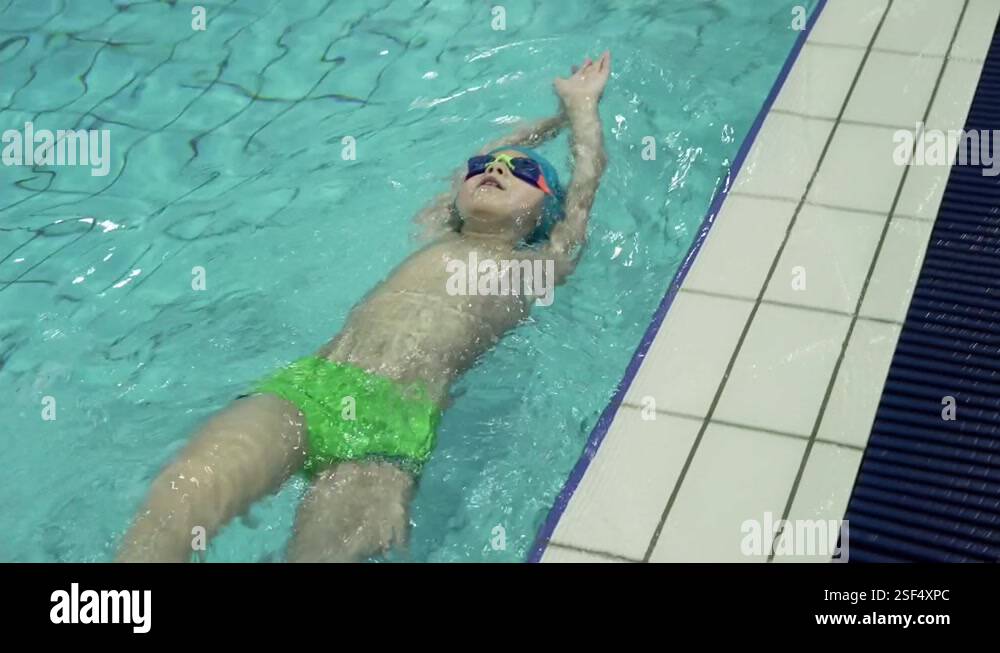 little caucasian boy wearing goggles swimming the backstroke in a pool ...