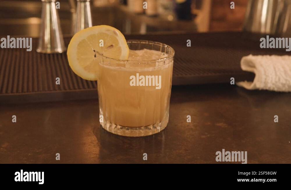 Cocktail glass sitting on bar is picked up toward camera by masculine ...