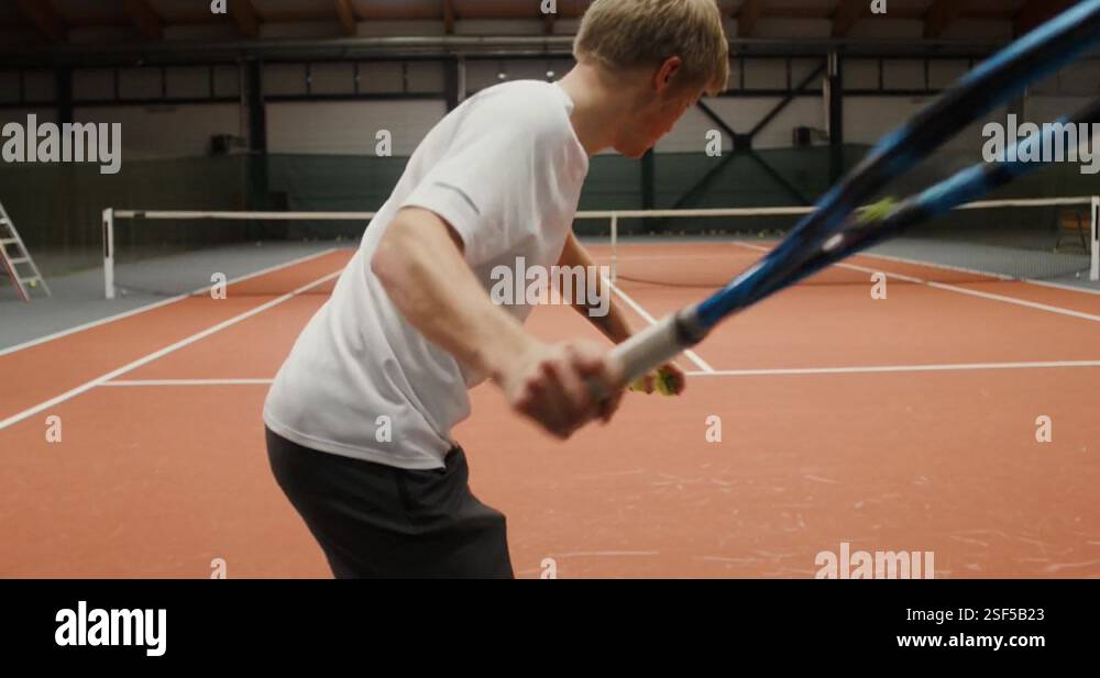A man trains in a tennis court alone, throwing tennis balls over the ...