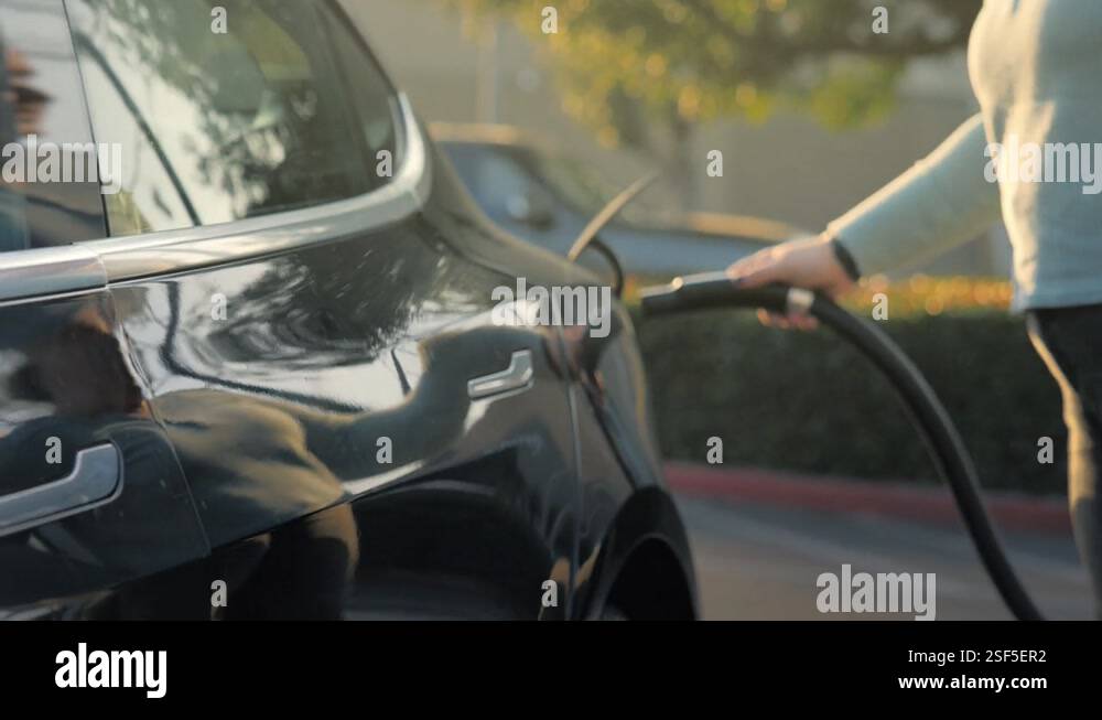 Person plugging electric charging plug cable into electric car charge ...