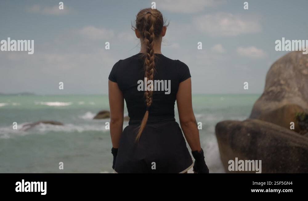 Athletically built female standing on the big stone by the ocean and ...