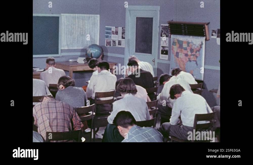 1950s: Classroom of students taking a test. Teacher walks down a row ...