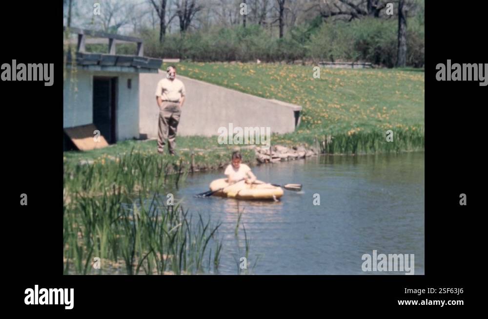 1950s: Boy rowing around pond in rubber dingy. Film slate. Father ...