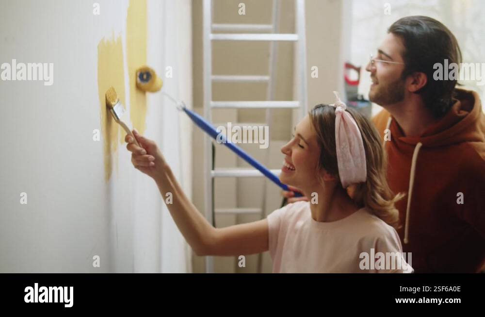 Young couple man and woman painting walls in yellow, making overhaul ...