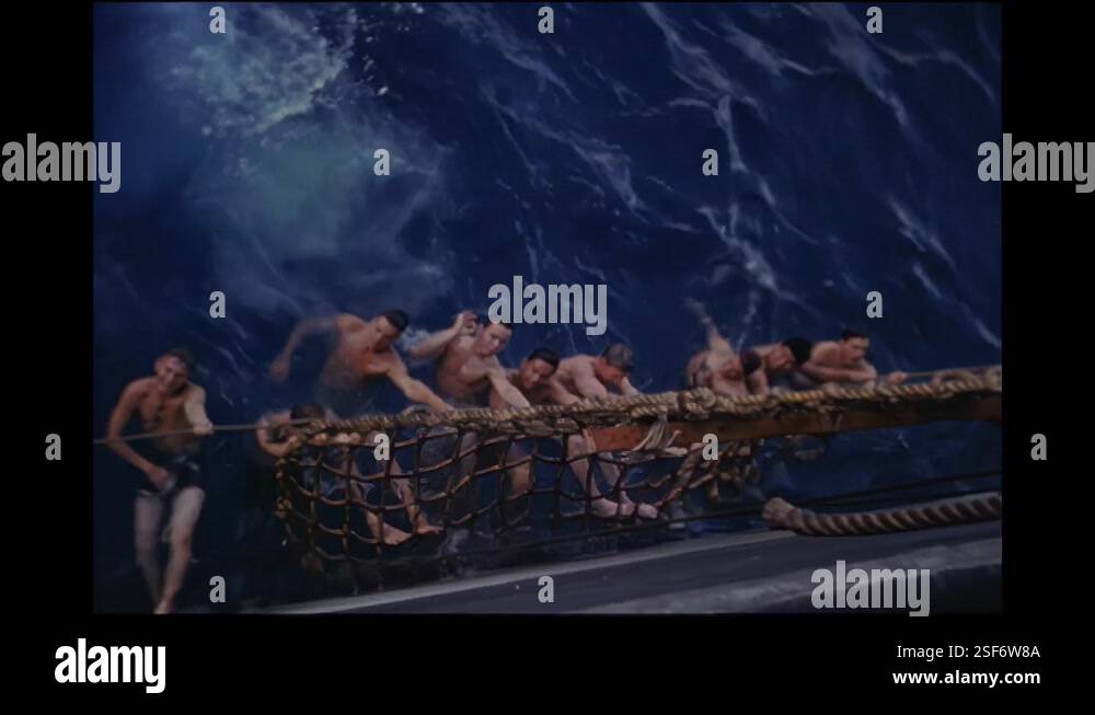 1940s: Sailors swim in the ocean. A row of sailors hang onto netting ...