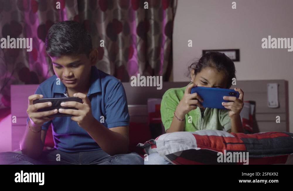 Siblings busy playing video game on mobile phone during night sleep ...