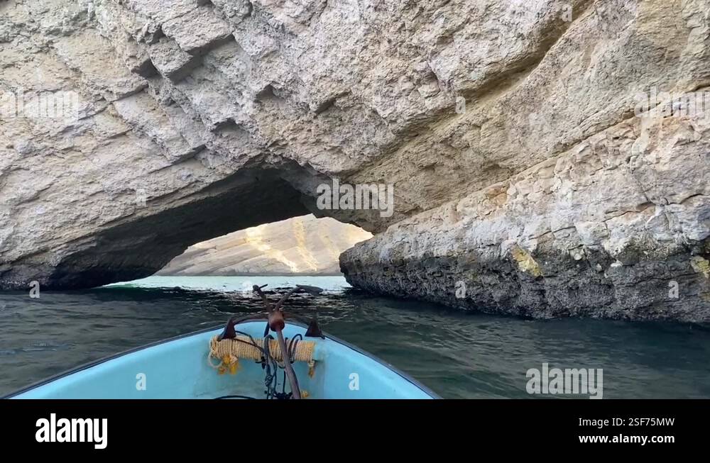 A ship with an anchor slowly passes under a natural stone arch near ...