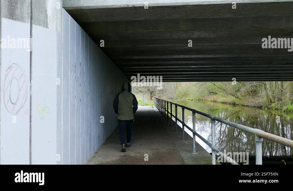 The back of an anonymous man walking under an overhead bridge, the ...