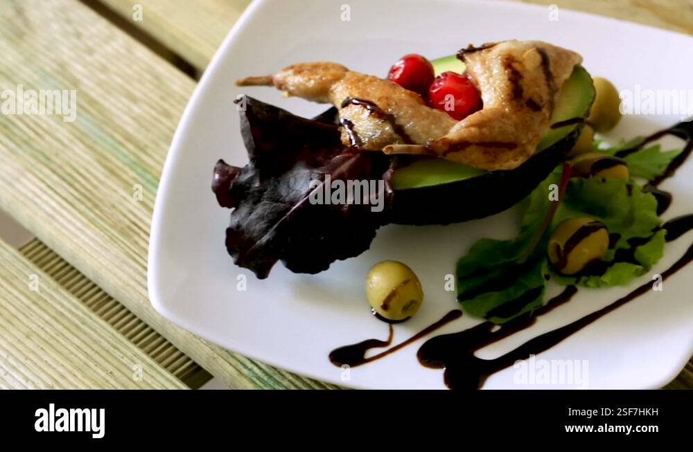 Ripe avocado with quail legs, cranberries, salad, olives and balsamic ...