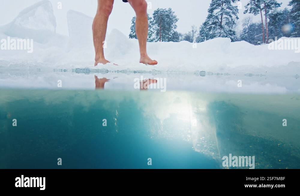 Winter swim. Young man walks barefoot on the snow to the open water to ...