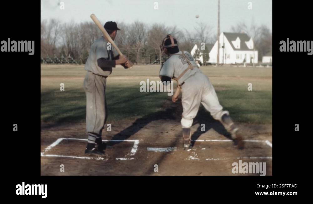 1940s: Rear view of baseball player at bat, pitcher throwing ball ...