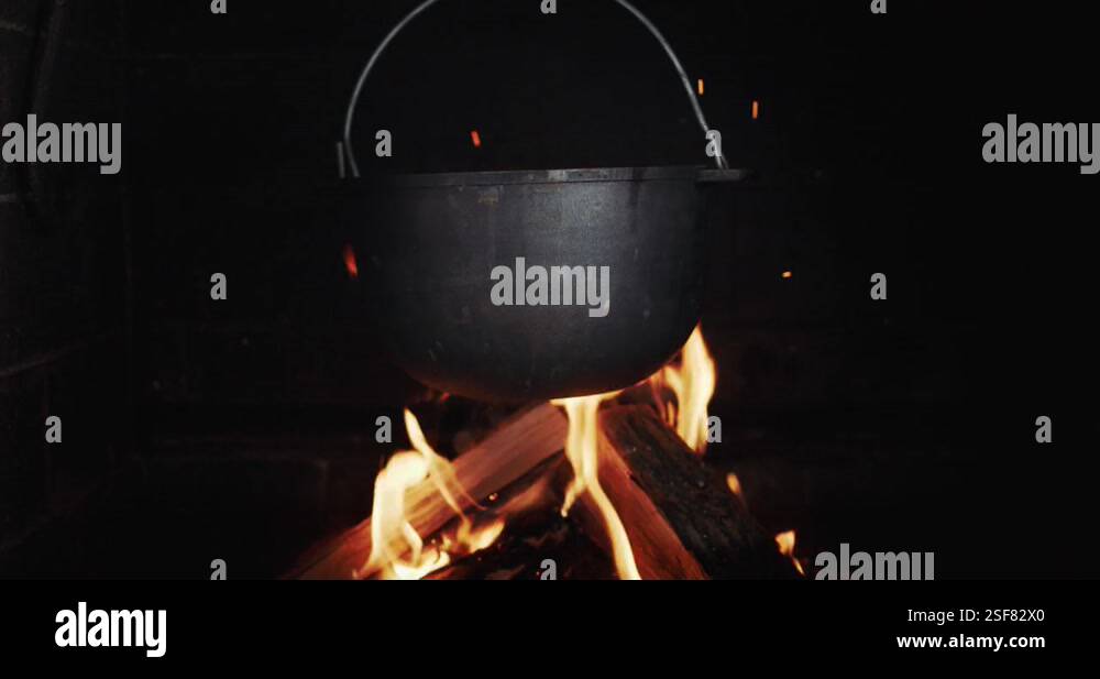 A cast-iron vat of boiling broth hangs in a wood-burning stove over an ...