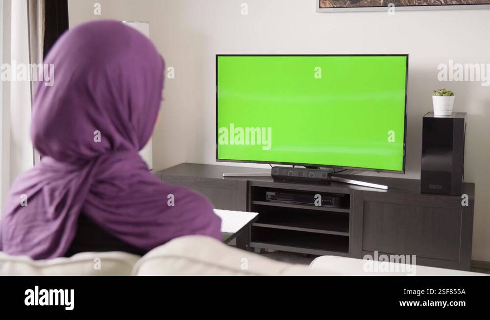 A Muslim woman watches TV with green screen and skips through channels ...