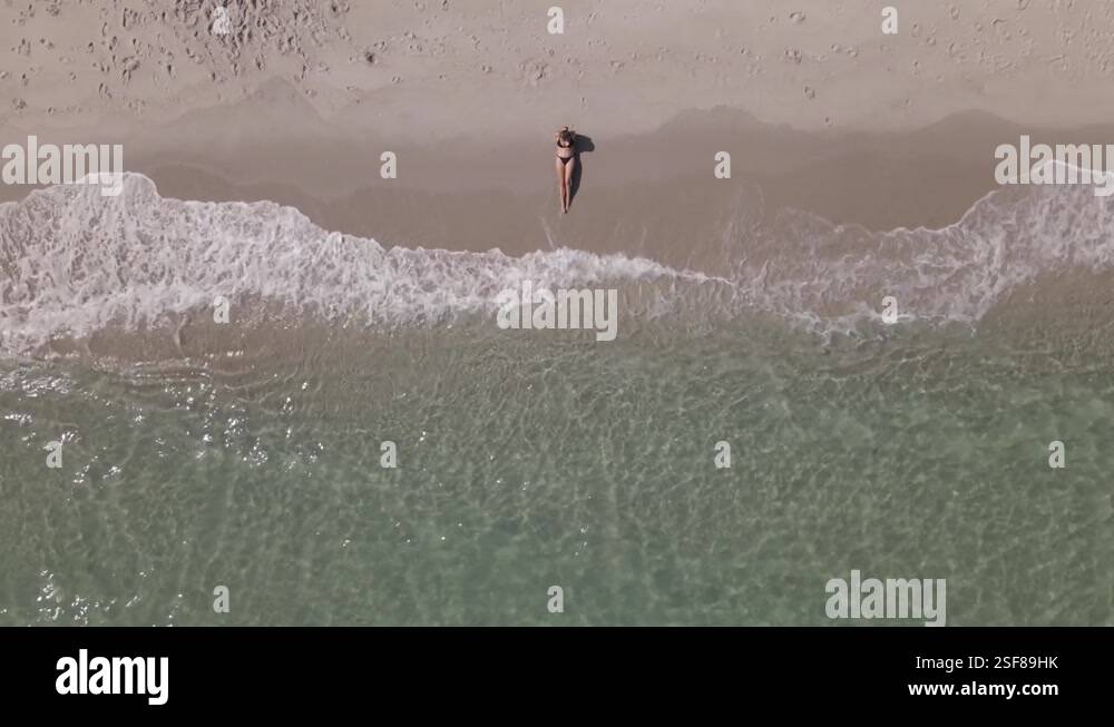 Overhead view of young bikini woman centered on beach with clear water Stock Video Footage - Alamy
