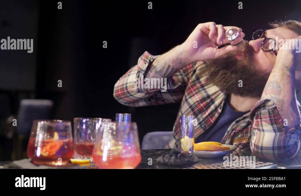 A very drunk young man is lying with his head on a table in a bar. A ...