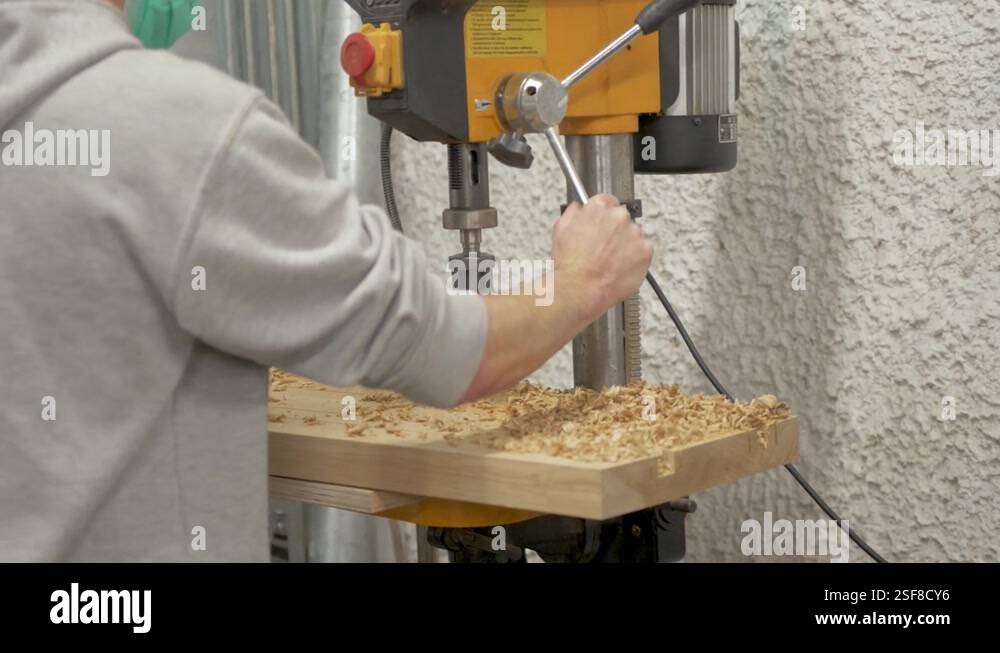 Young man using pillar drill drilling holes in white oak slab. MEDIUM ...