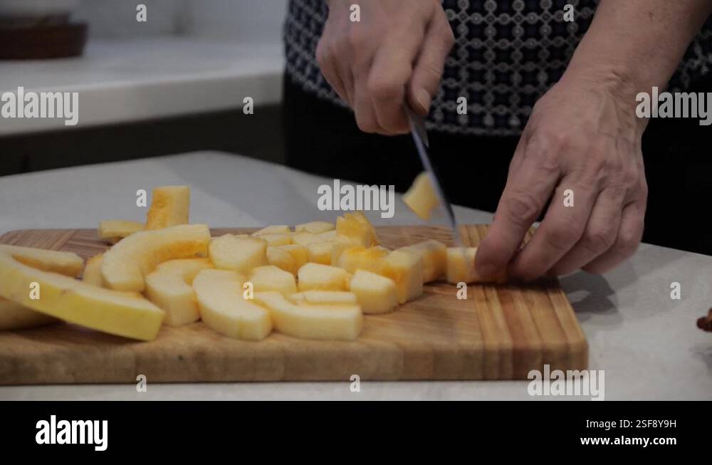 Slicing zucchini on a wooden board on a white table with a large chef's ...