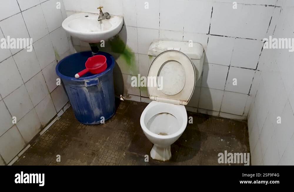 A public toilet restroom bathroom with a leaking running tap, water on ...