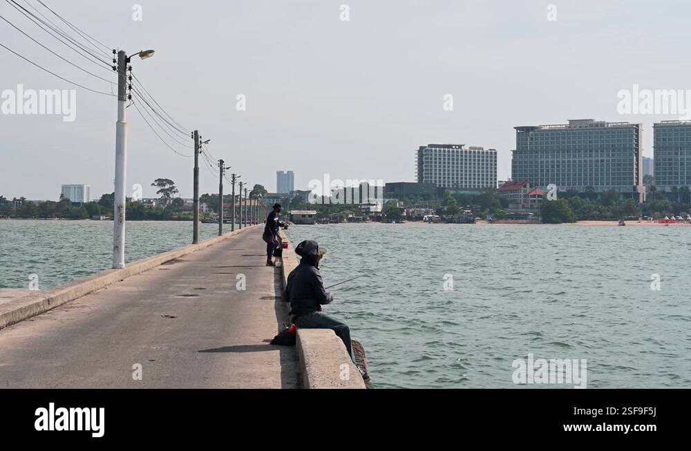 A man sitting reeling in the lure at the Pattaya Fishing Dock, Chonburi ...