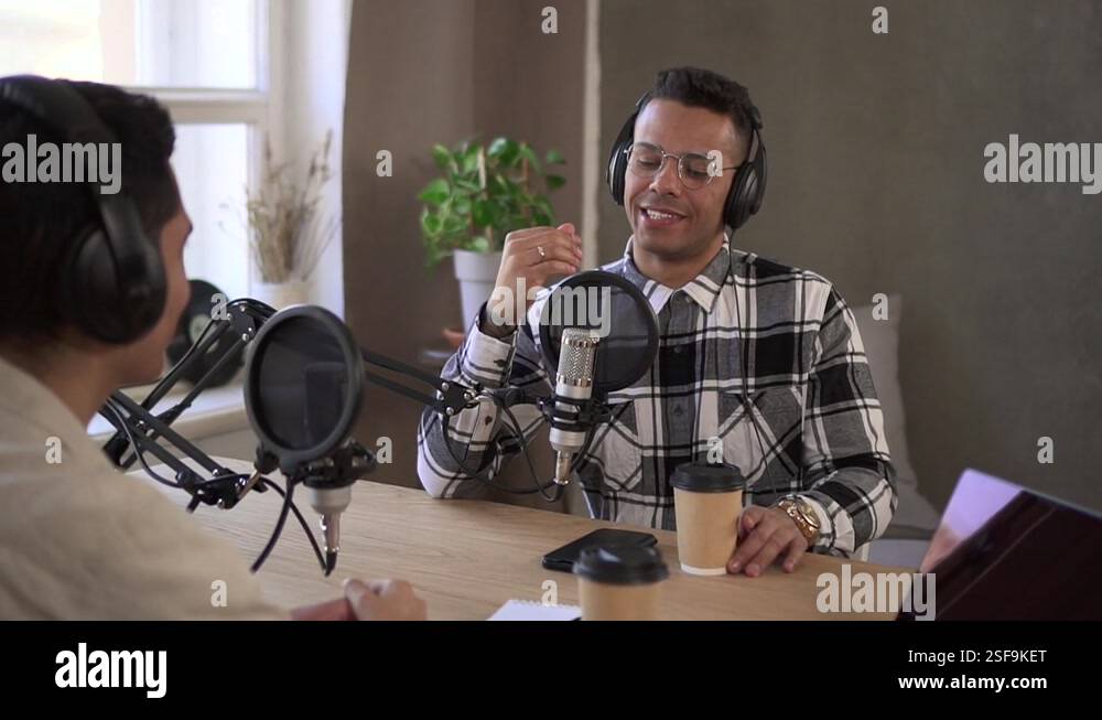 Two young men recording podcast and talking at table in front of ...