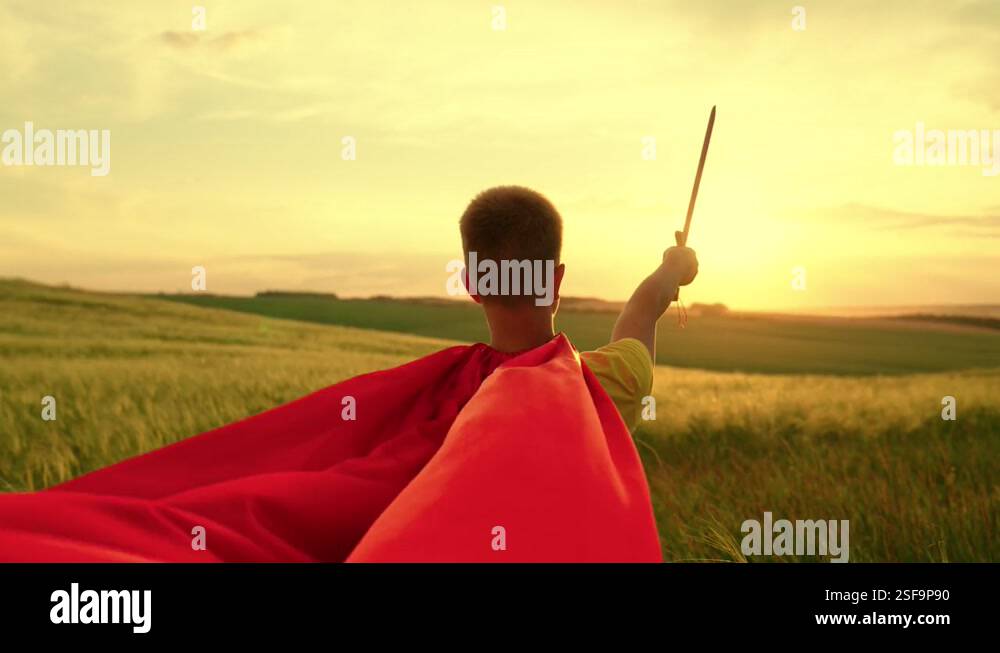 Boy in red cloak stands with sword raised in his hand up sword, on ...