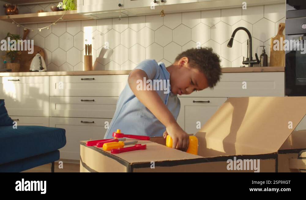 Positive school age African boy repairing diy cardboard car with toy ...