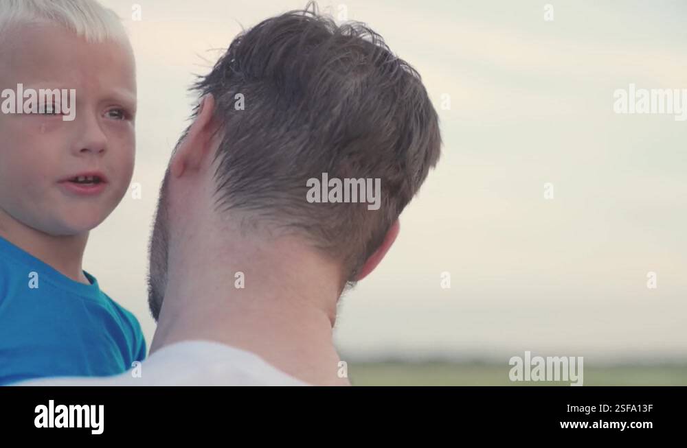 Child cries in park in arms of his father. Father comforts child ...