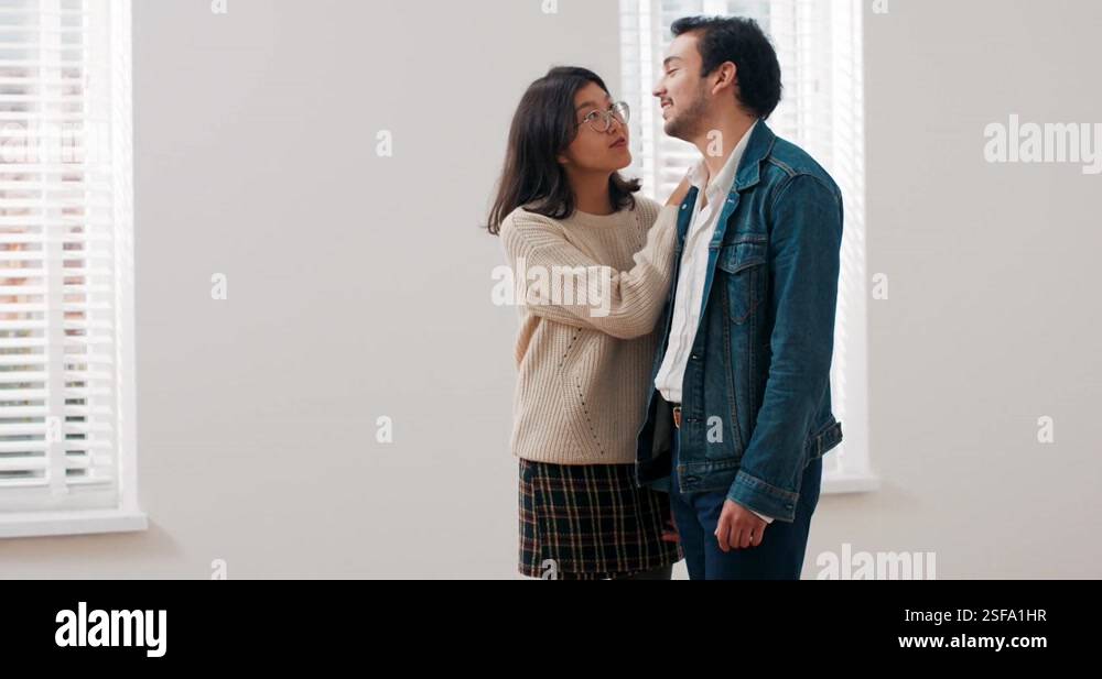 A young married couple stands in an empty purchased apartment, embrace ...