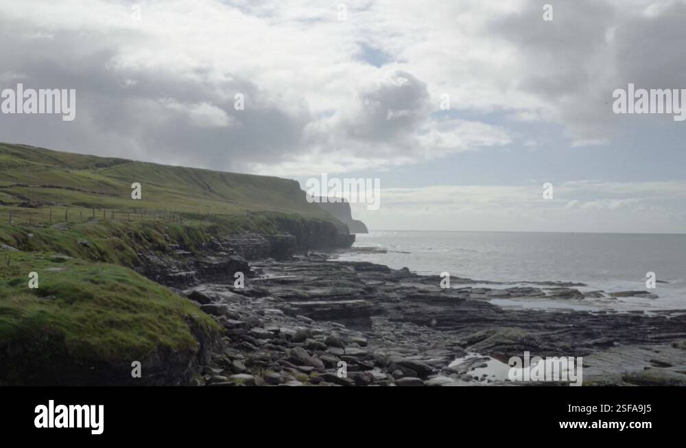 Light rain falls on green and rocky Irish coastal cliffs in summer ...