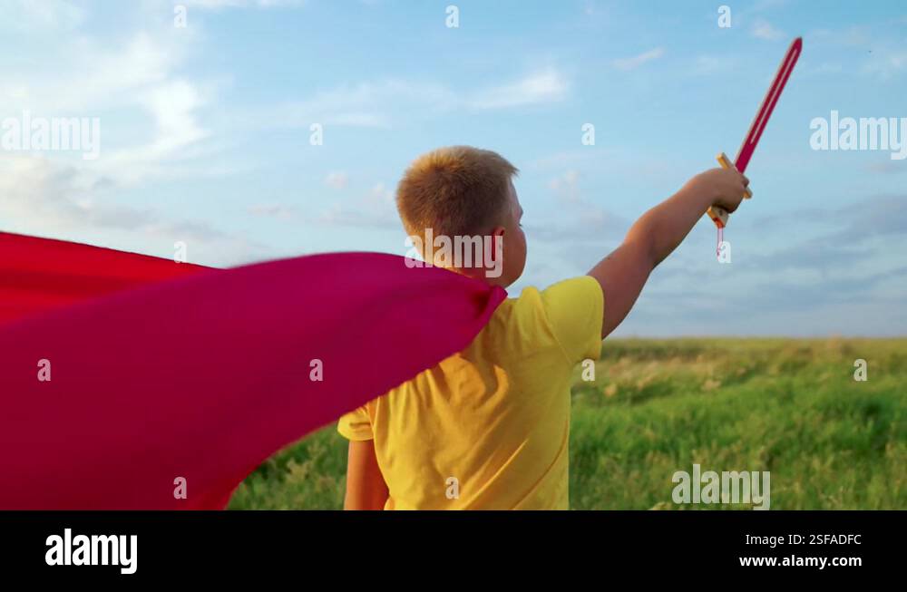 Boy, child in red cloak go with sword raised in his hand up sword, on ...