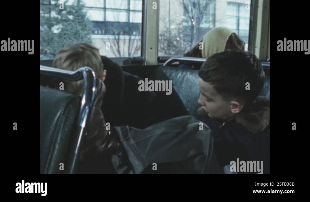1950s: Little boys sit on bus and talk. Boy pushes on bus seat with ...
