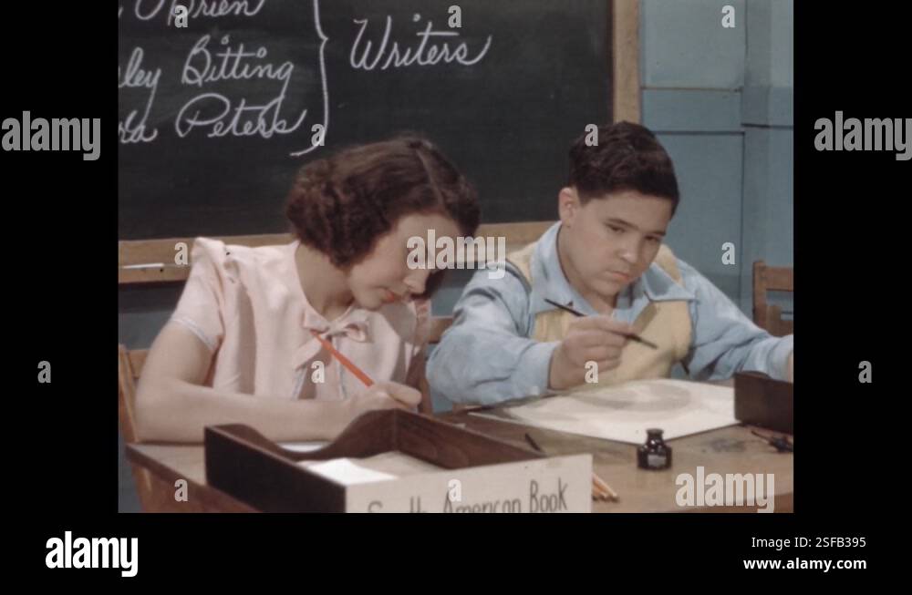 1940s: Boy and girl write on paper and talk at desk in classroom Stock ...