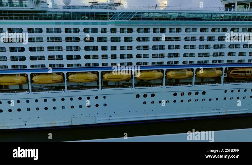 Side view of a huge luxury cruise ship sailing from port with lifeboats ...