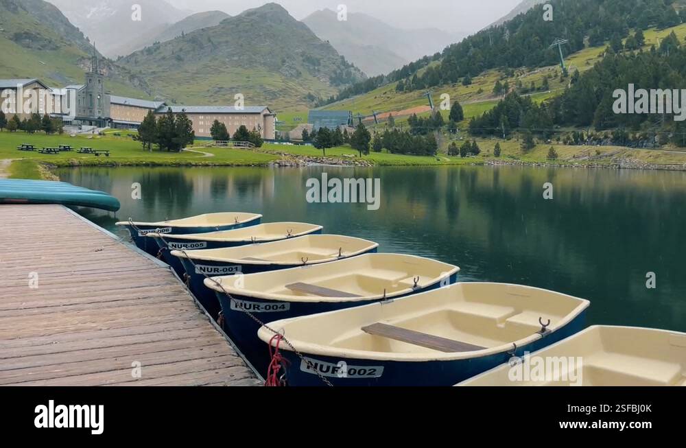 Small boats moored to a wooden dock on a rainy day, in a mountain ...