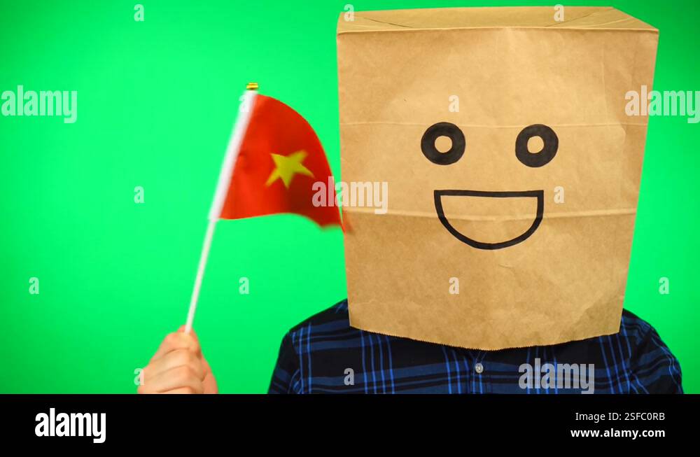 Portrait of man with paper bag on head waving Vietnamese flag with ...