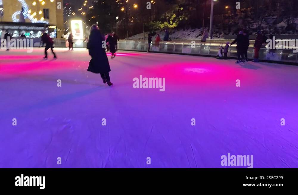 People skating on an ice skating rink with colorful light in open air ...