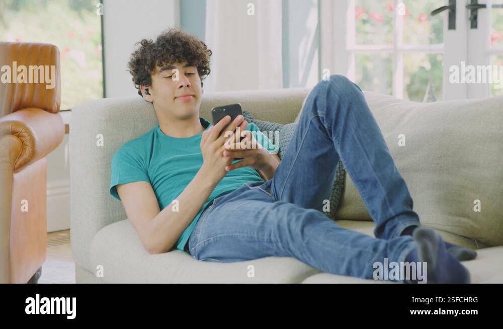 Teenage Boy Wearing Wireless Earbuds Posing For Selfie On Sofa At Home ...