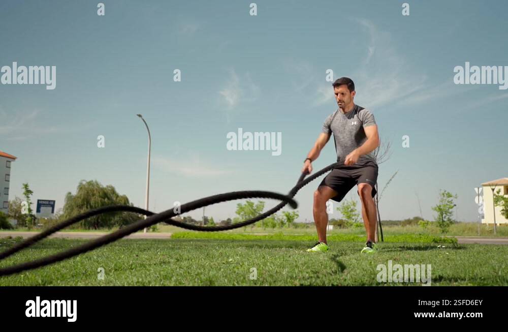 Muscular caucasian athlete makes waves with a battle rope on the grass ...