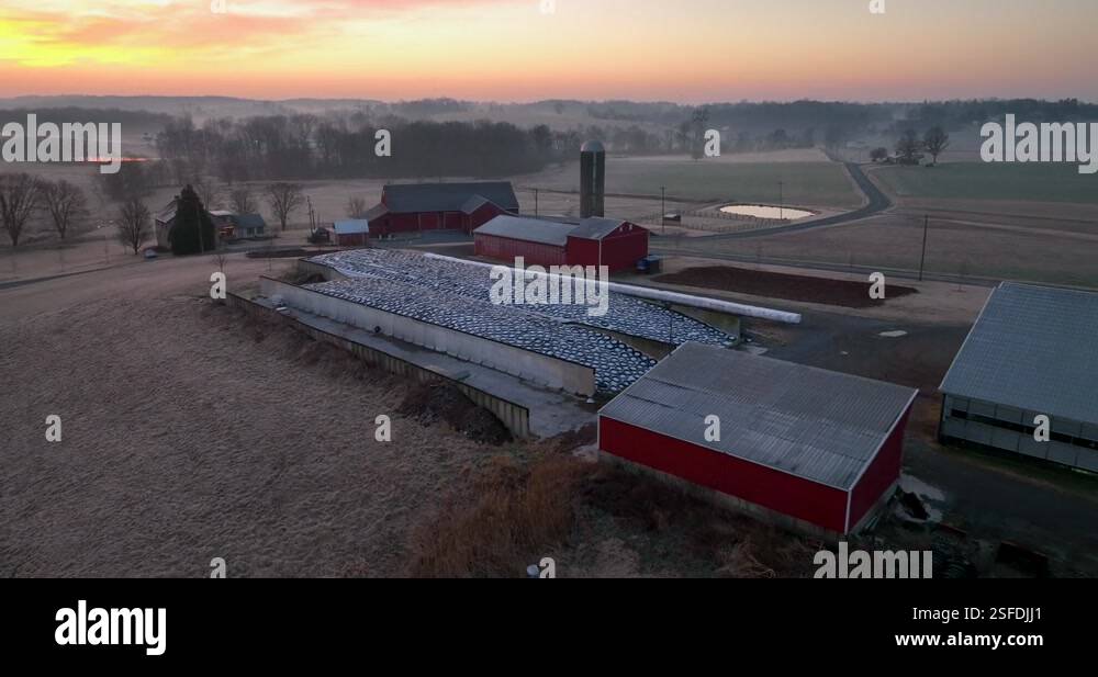 Rising aerial of rural farm scene in USA. Silage pile, barns and dairy ...