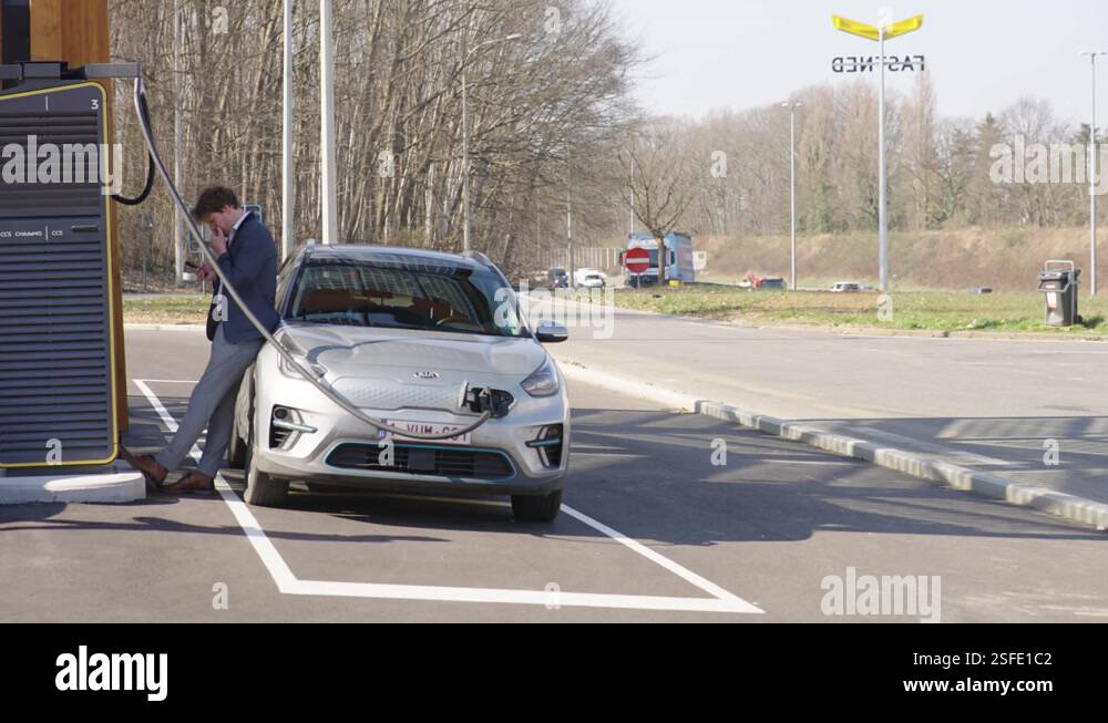 A lone man on his mobile device leans against his electric car at a ...