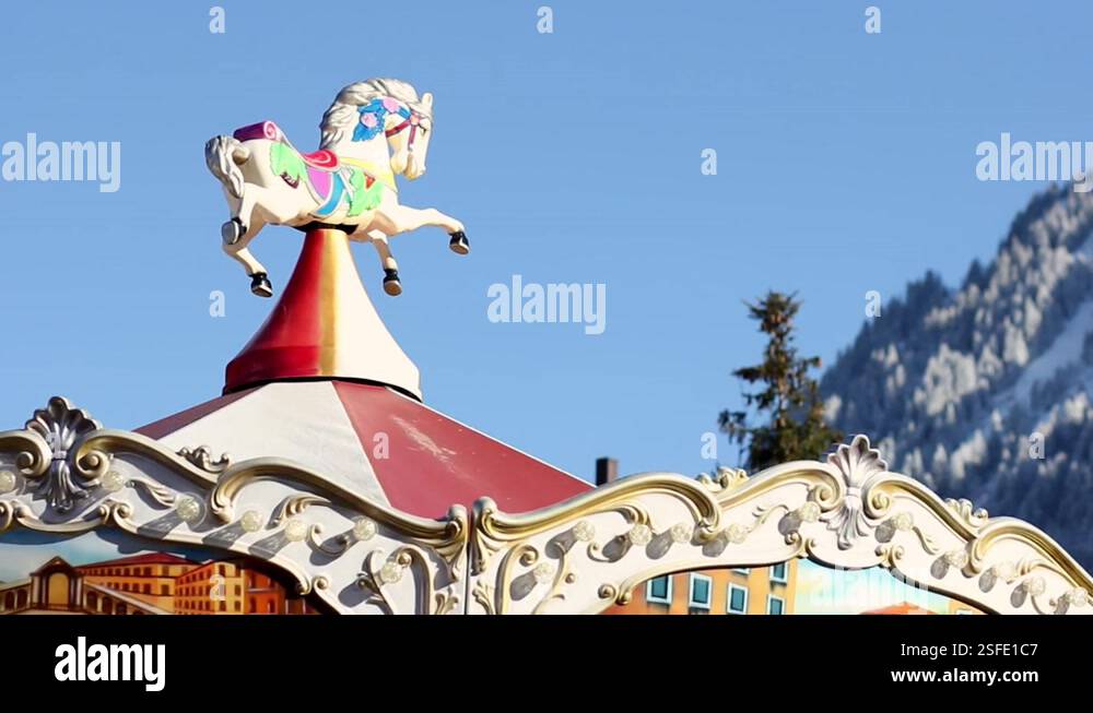 Top horse of a carousel turning with snowed white mountains at the ...