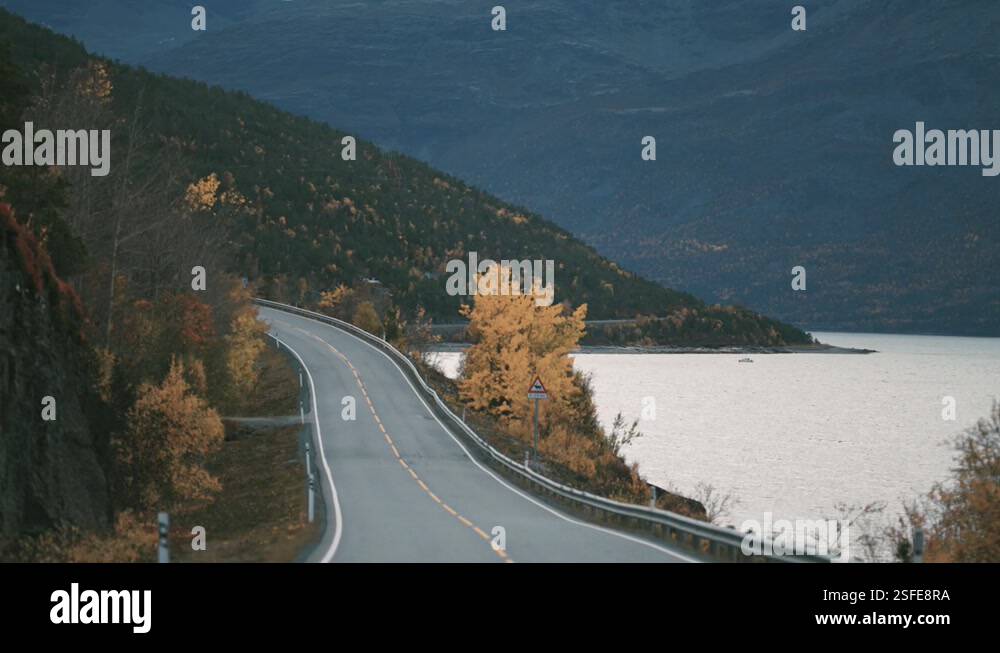Narrow two-lane road snaking along the fjord. Snow-capped mountains on ...