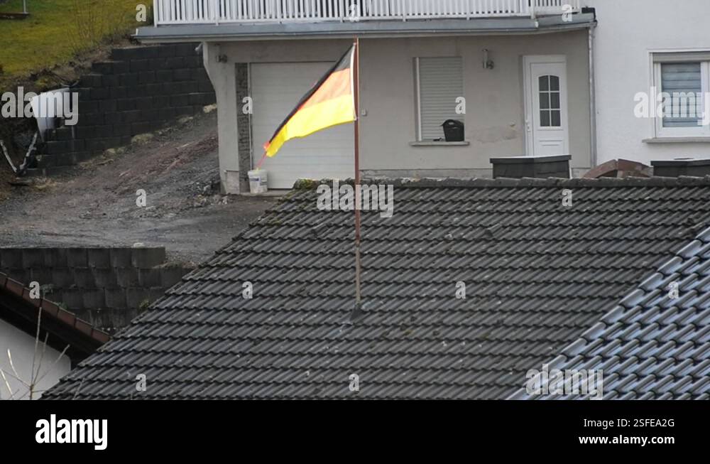 A faded German flag on a pole attached to a tile roof waving in the ...