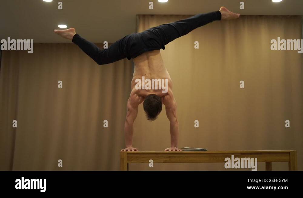 A muscular man keeps balance on one hand and uses laptop. Concept of ...