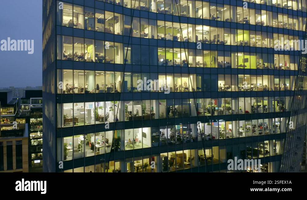 Facade of a skyscraper at night with office windows and people working ...
