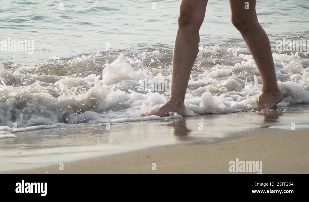 Young woman's legs close up walking and splashing on the sea shore with ...