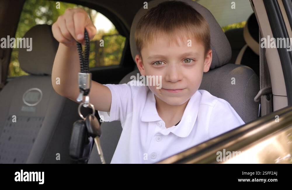 A little boy is sitting in a new car in the front seat with keys in his ...